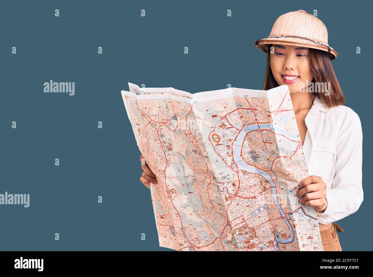 Young beautiful chinese girl wearing explorer hat holding map looking ...