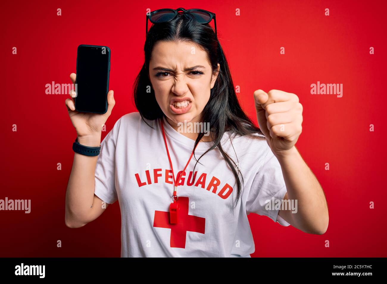 Young lifeguard woman showing smartphone screen over red background ...