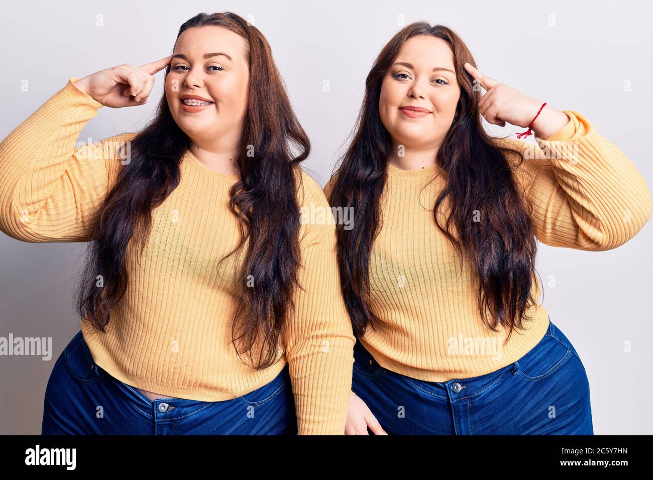 Young plus size twins wearing casual clothes smiling pointing to head ...