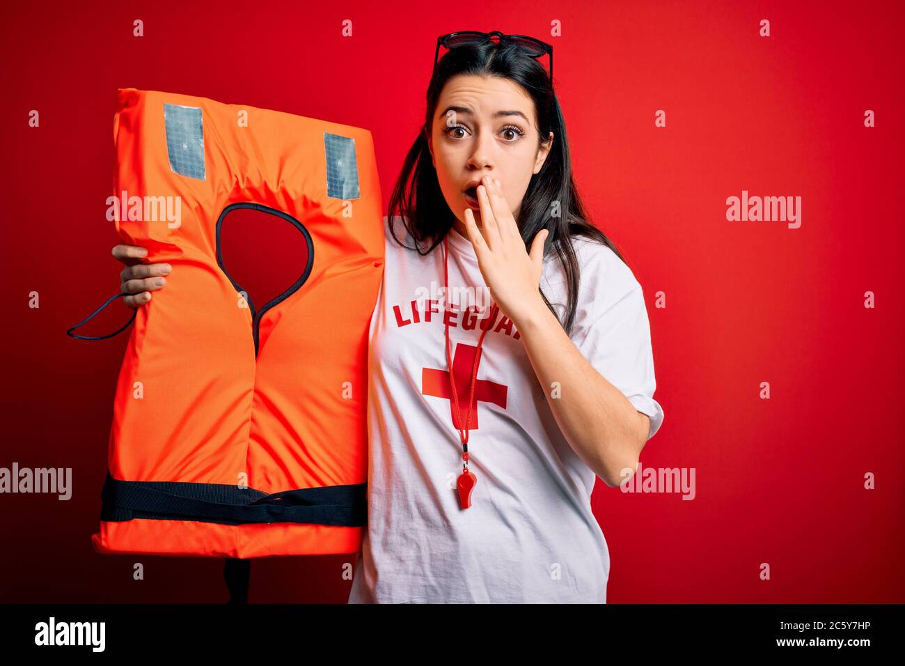 Young lifeguard woman holding rescue lifejacket over red background ...