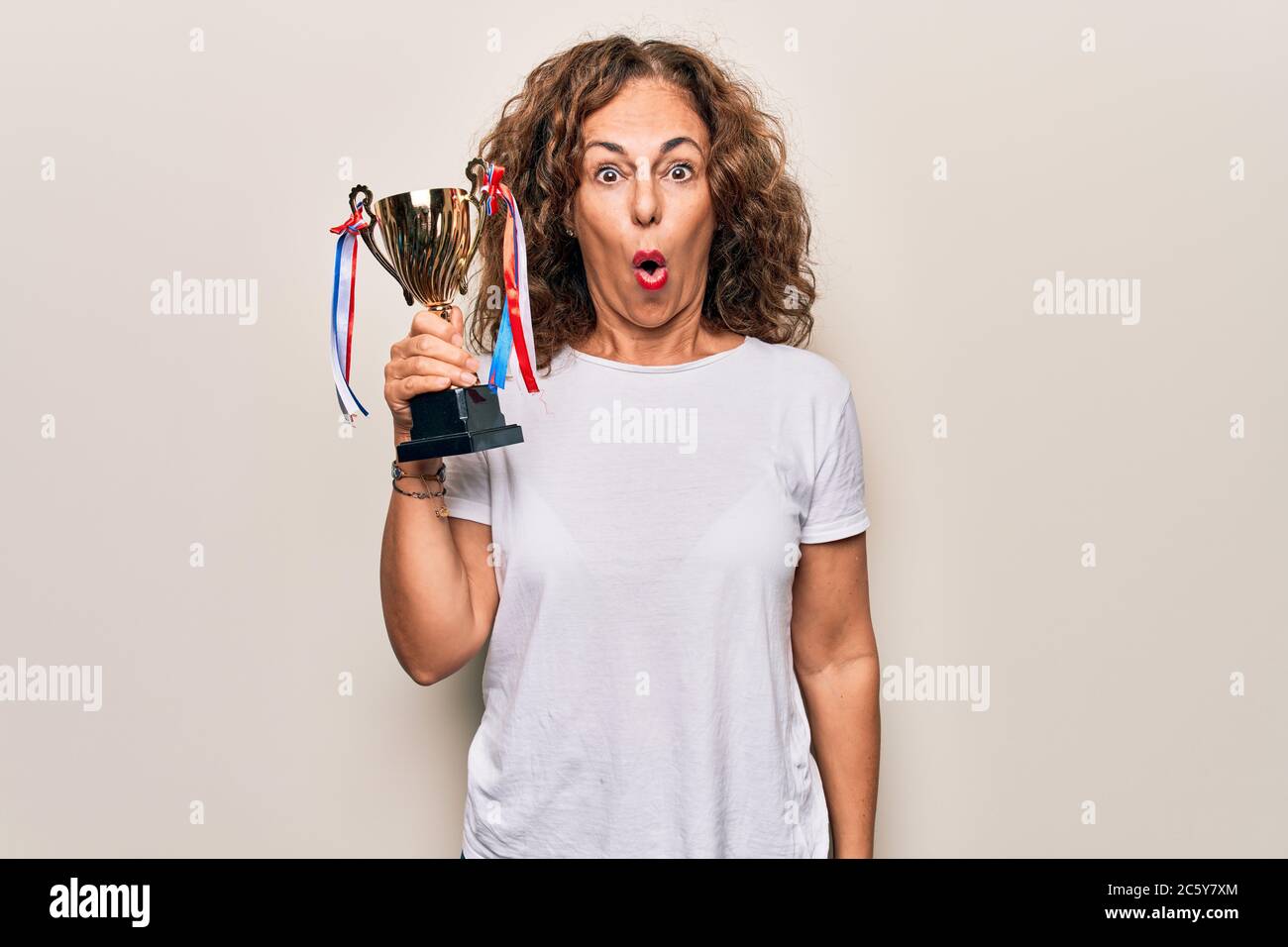 Middle age beautiful successful woman holding trophy for victory over ...