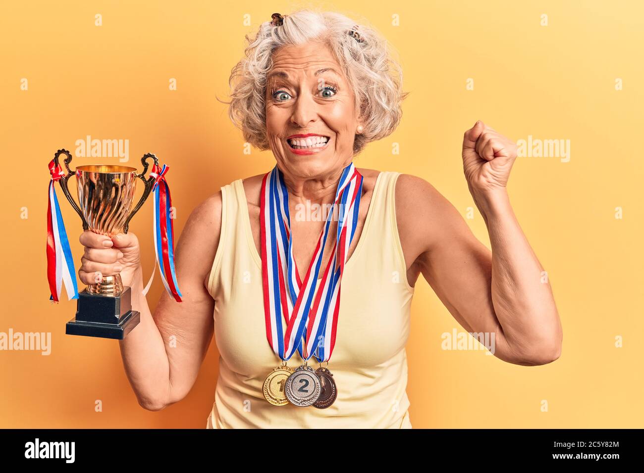 Senior grey-haired woman holding champion trophy wearing medals ...