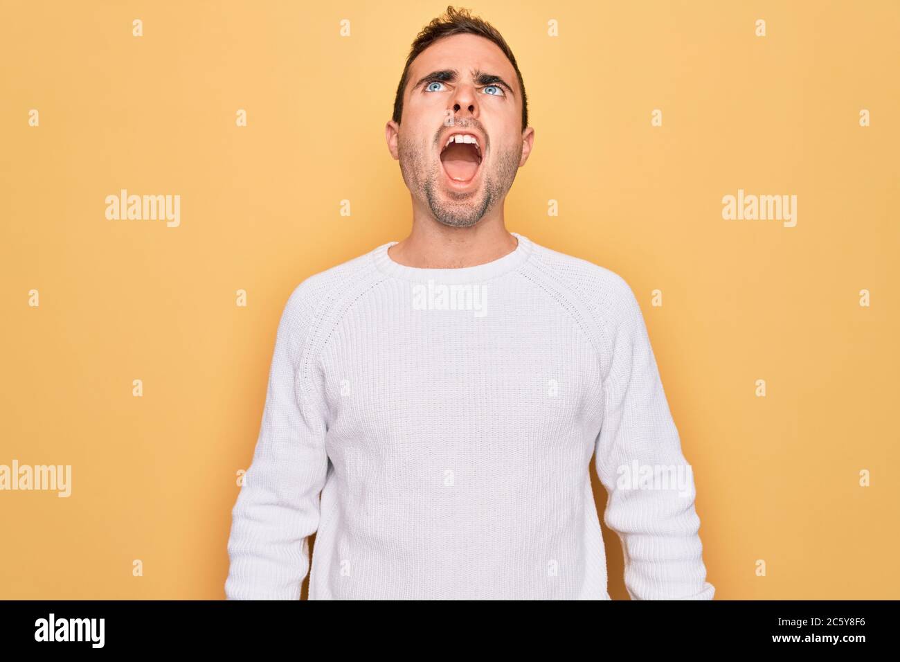 Young handsome man with blue eyes wearing casual sweater standing over ...