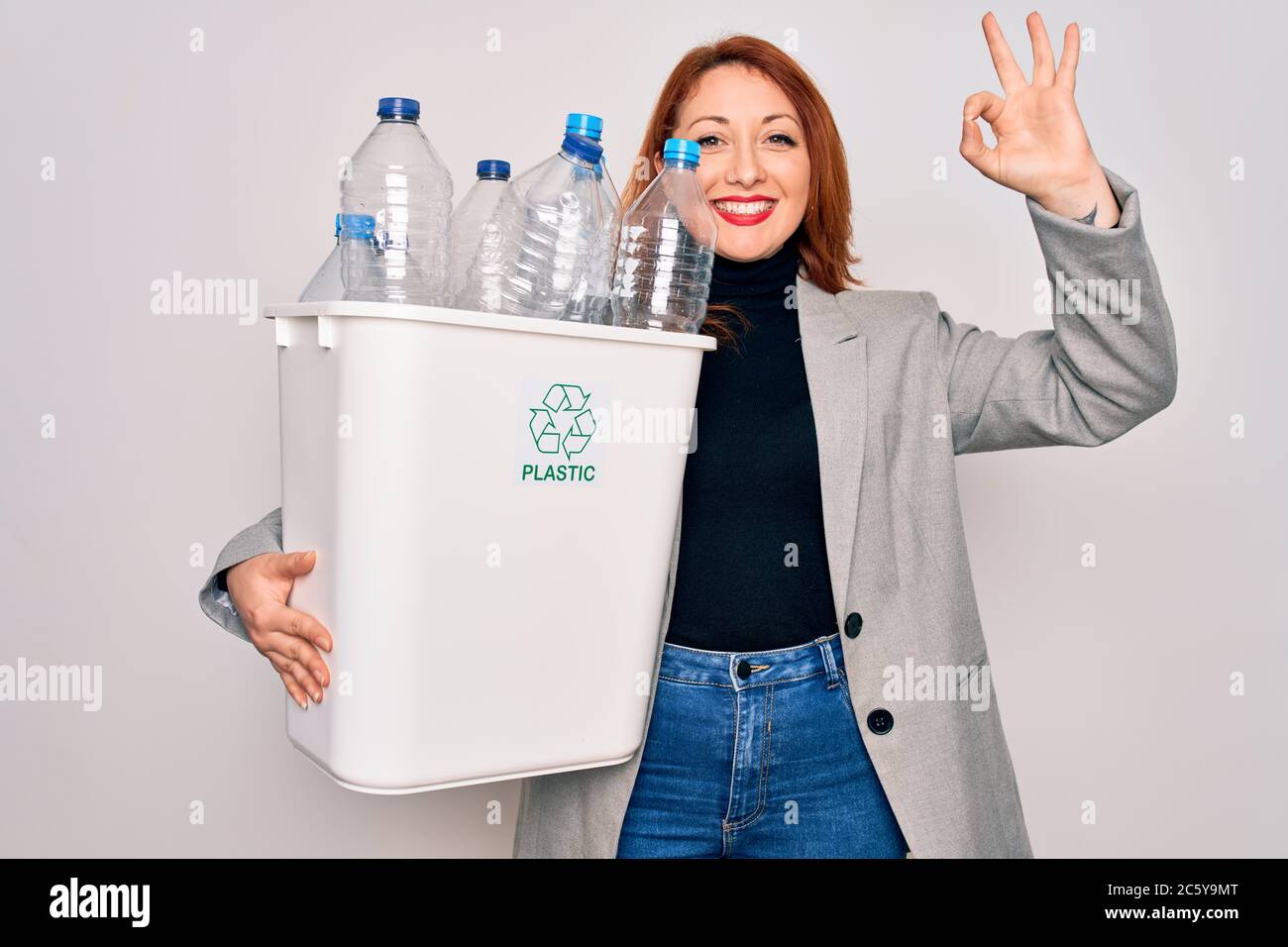Young beautiful redhead woman recycling holding trash can with plastic ...
