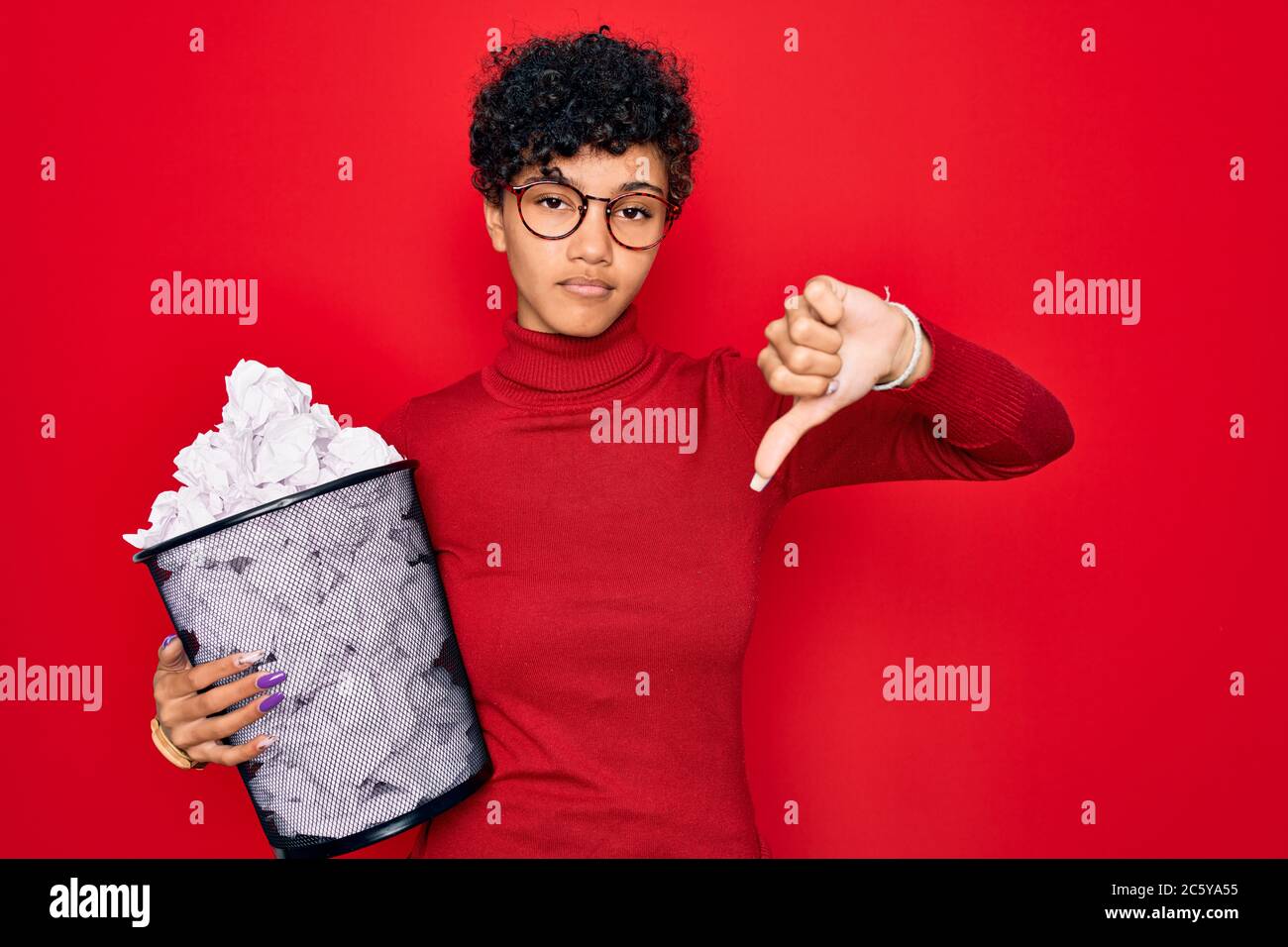 Young beautiful african american afro woman holding full paper bin with ...