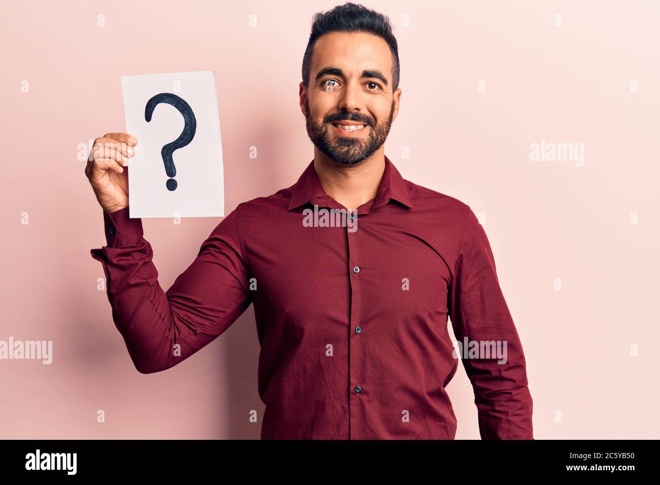 Young hispanic man holding question mark looking positive and happy ...