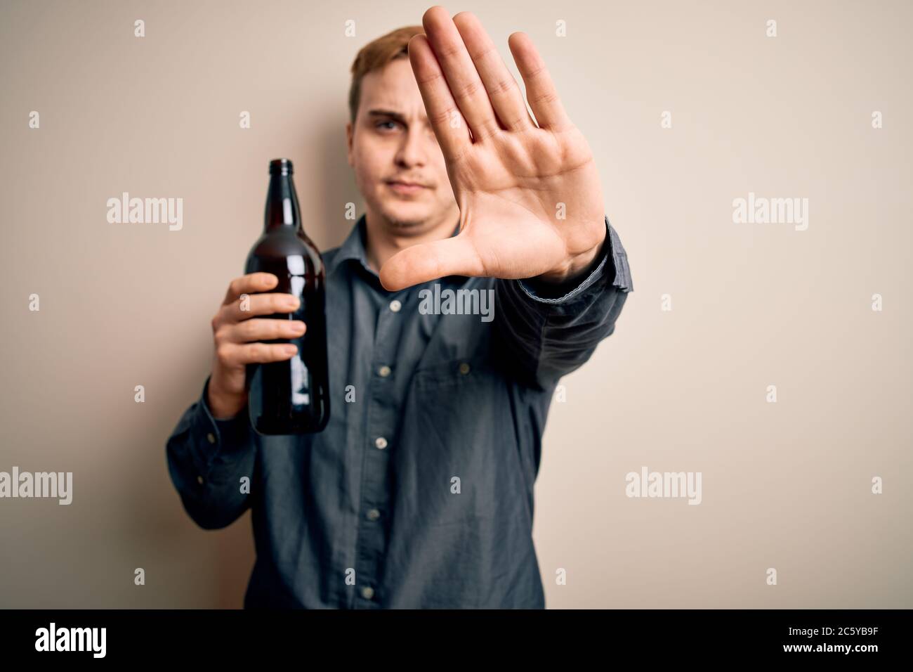 Young handsome redhead man drinking bottle of beer over isolated white ...