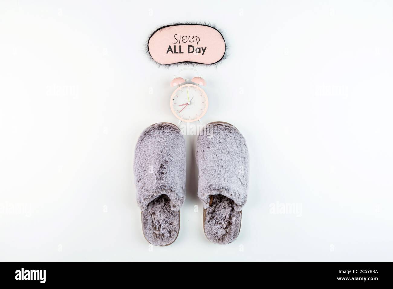 Flat lay with Soft fluffy slippers gray color, blindfold and pink alarm ...