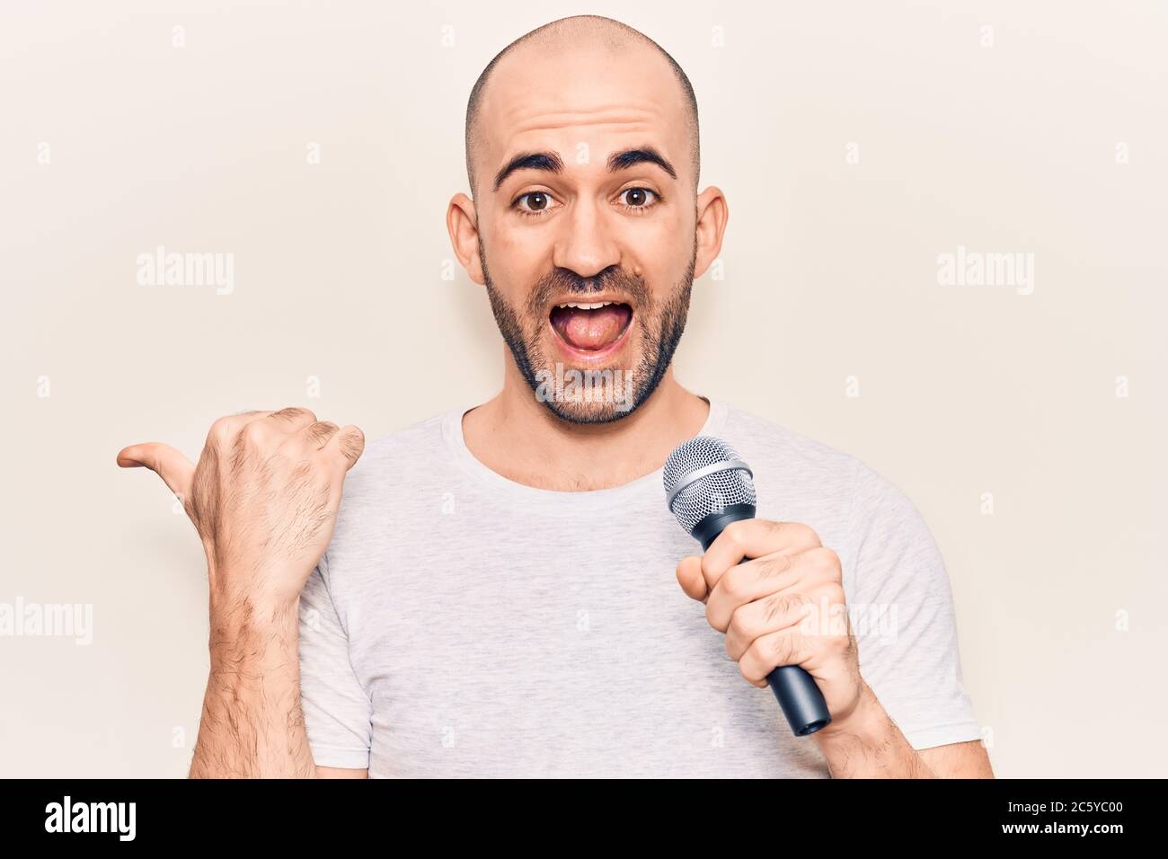 Young handsome bald man singing song using microphone pointing thumb up ...