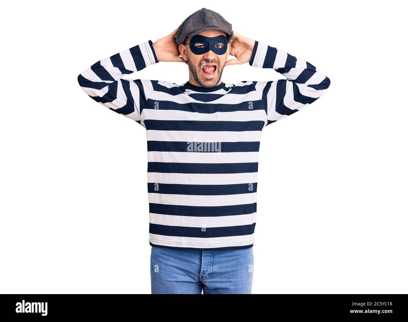 Young handsome man wearing burglar mask crazy and scared with hands on ...