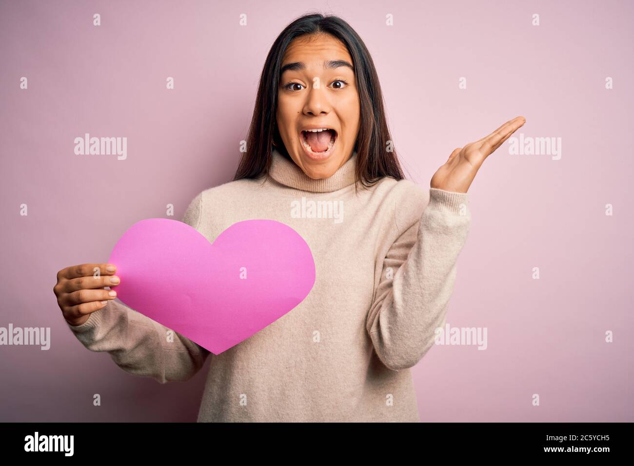Young beautiful asian woman holding pink heart standing over isolated ...