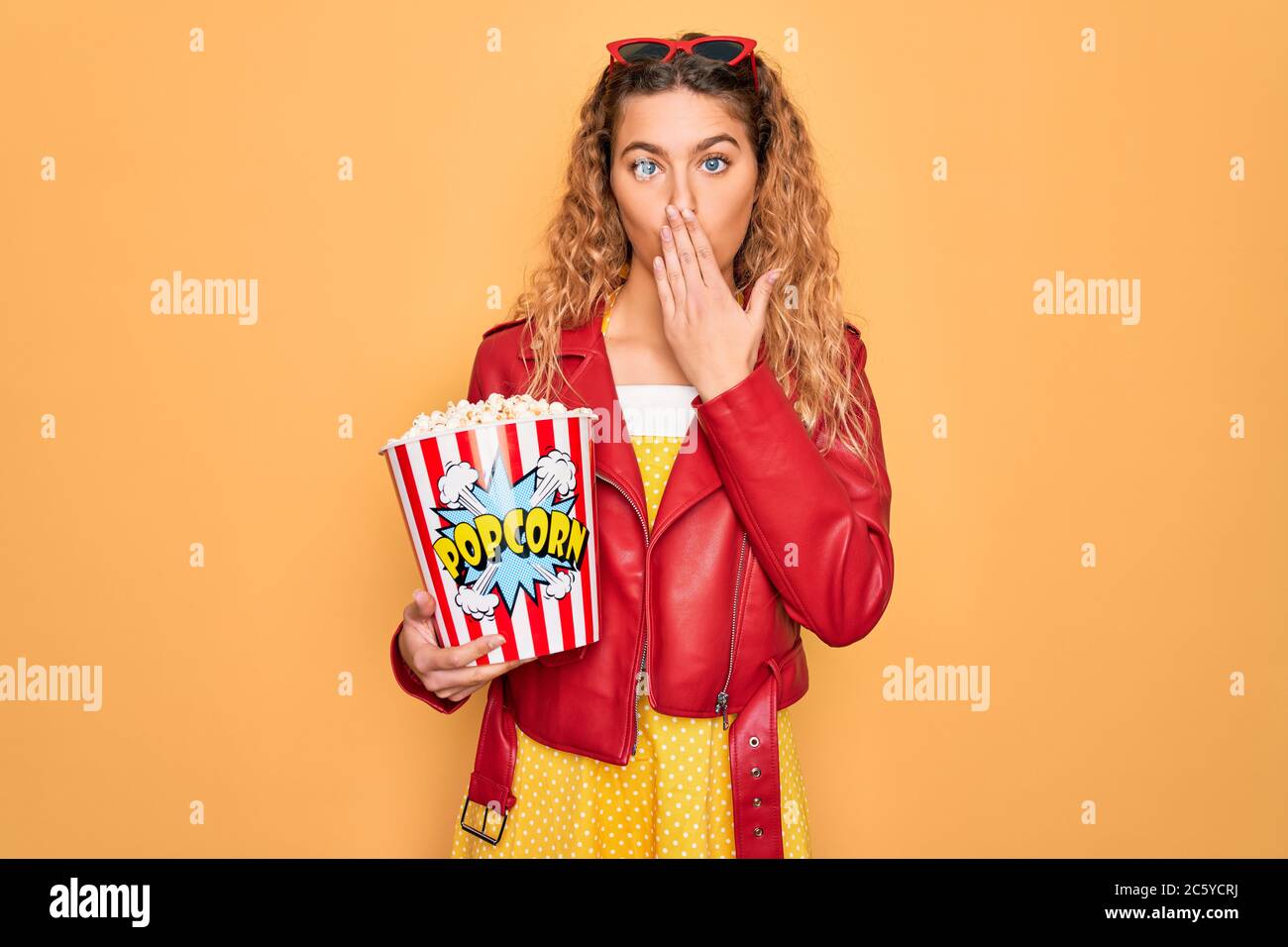 Beautiful blonde woman with blue eyes eating salty popcorn snack over ...