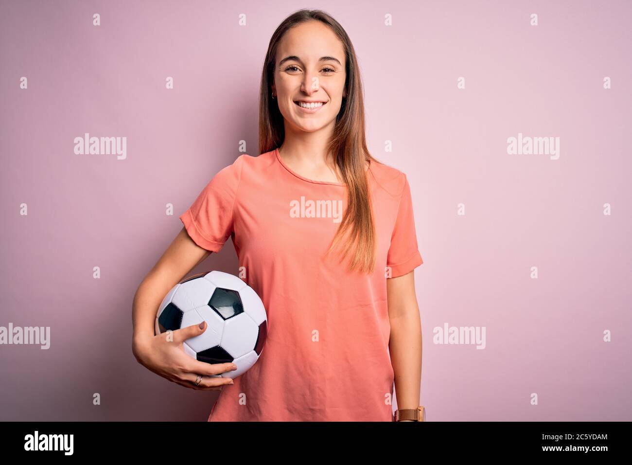 Young beautiful player woman playing soccer holding football ball over ...