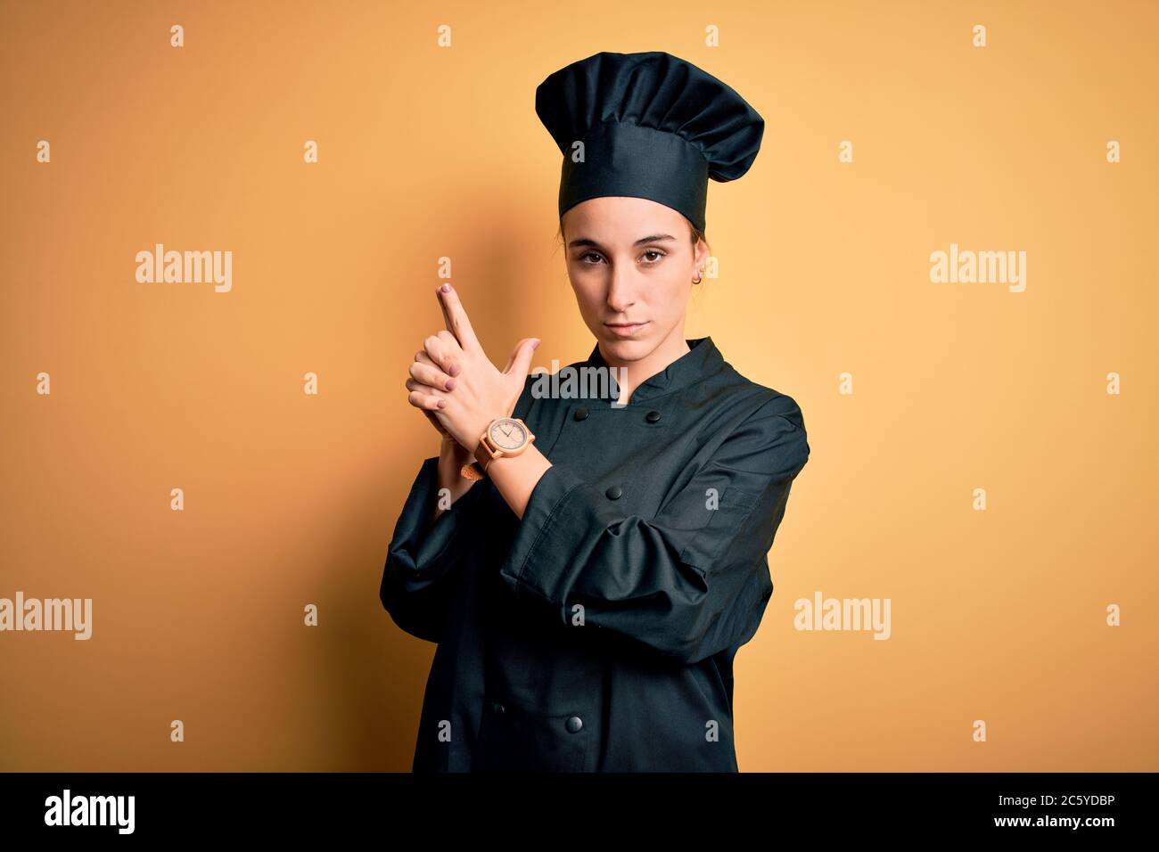 Young beautiful chef woman wearing cooker uniform and hat standing over ...