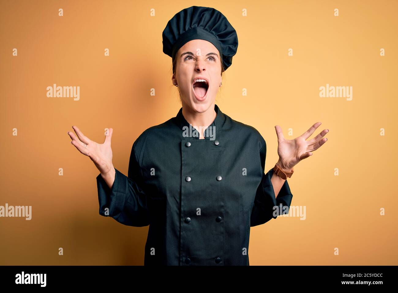 Young beautiful chef woman wearing cooker uniform and hat standing over ...