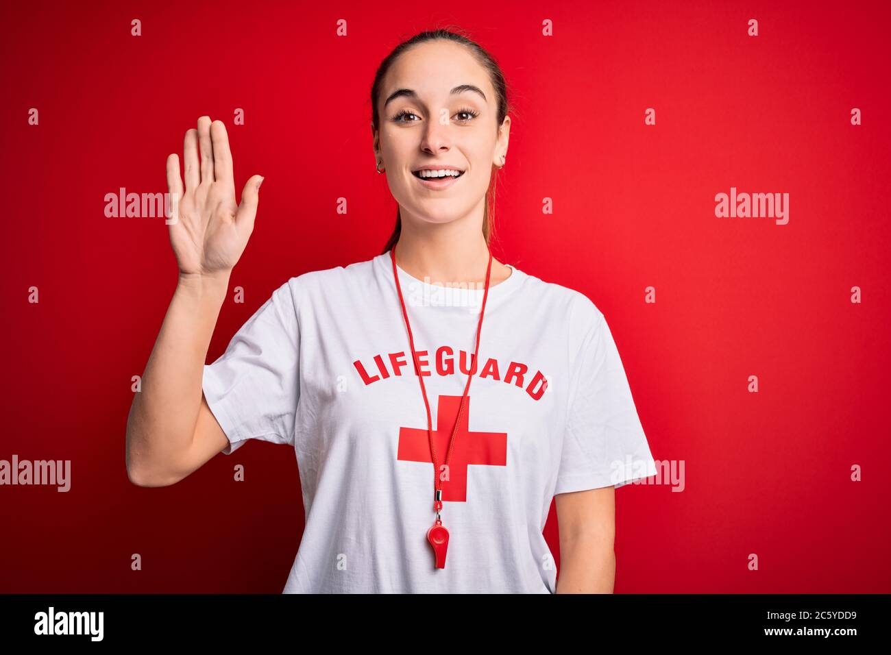 Beautiful lifeguard woman wearing t-shirt with red cross using whistle ...