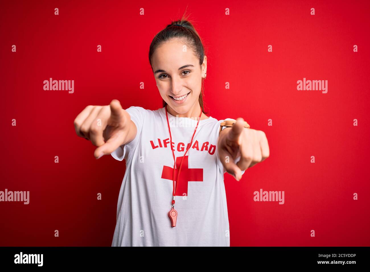 Beautiful lifeguard woman wearing t-shirt with red cross using whistle ...