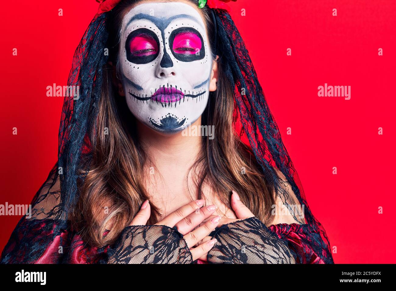 Young woman wearing day of the dead costume over red smiling with hands ...