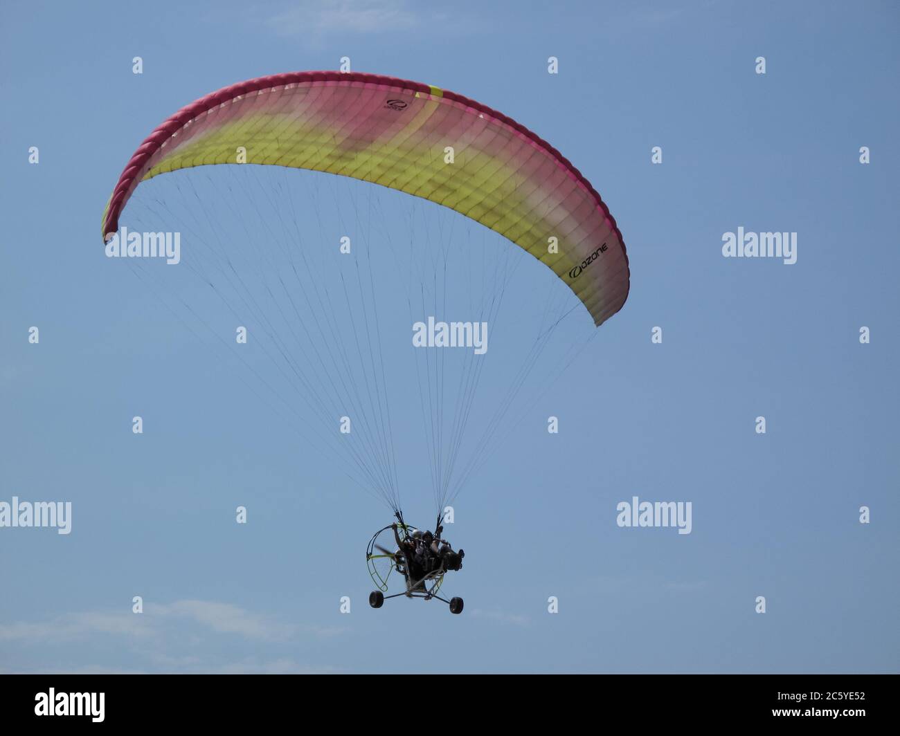 A paraglider flies in the sky under a multi-colored paraglider ...