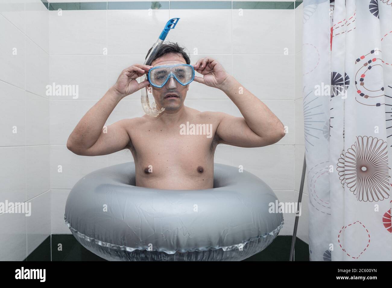 Man with gray swimming ring putting on goggles and snorkel and standing ...