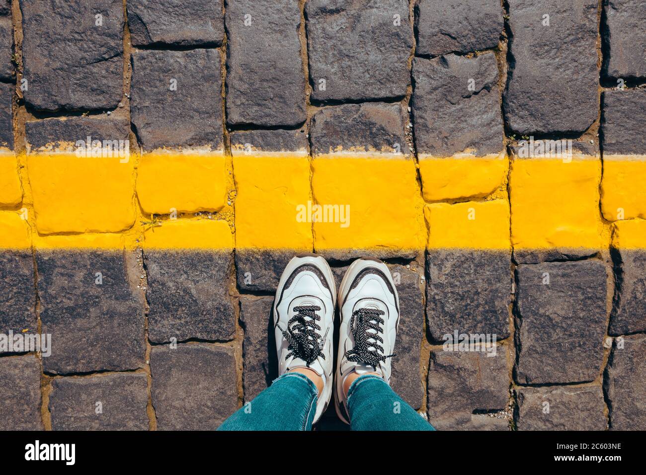 women's feet in white sneakers stand on the pavement behind the yellow ...