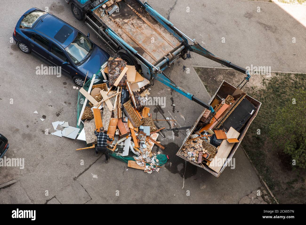 Garbage container fell over blue car. Driver tries to put trash back ...