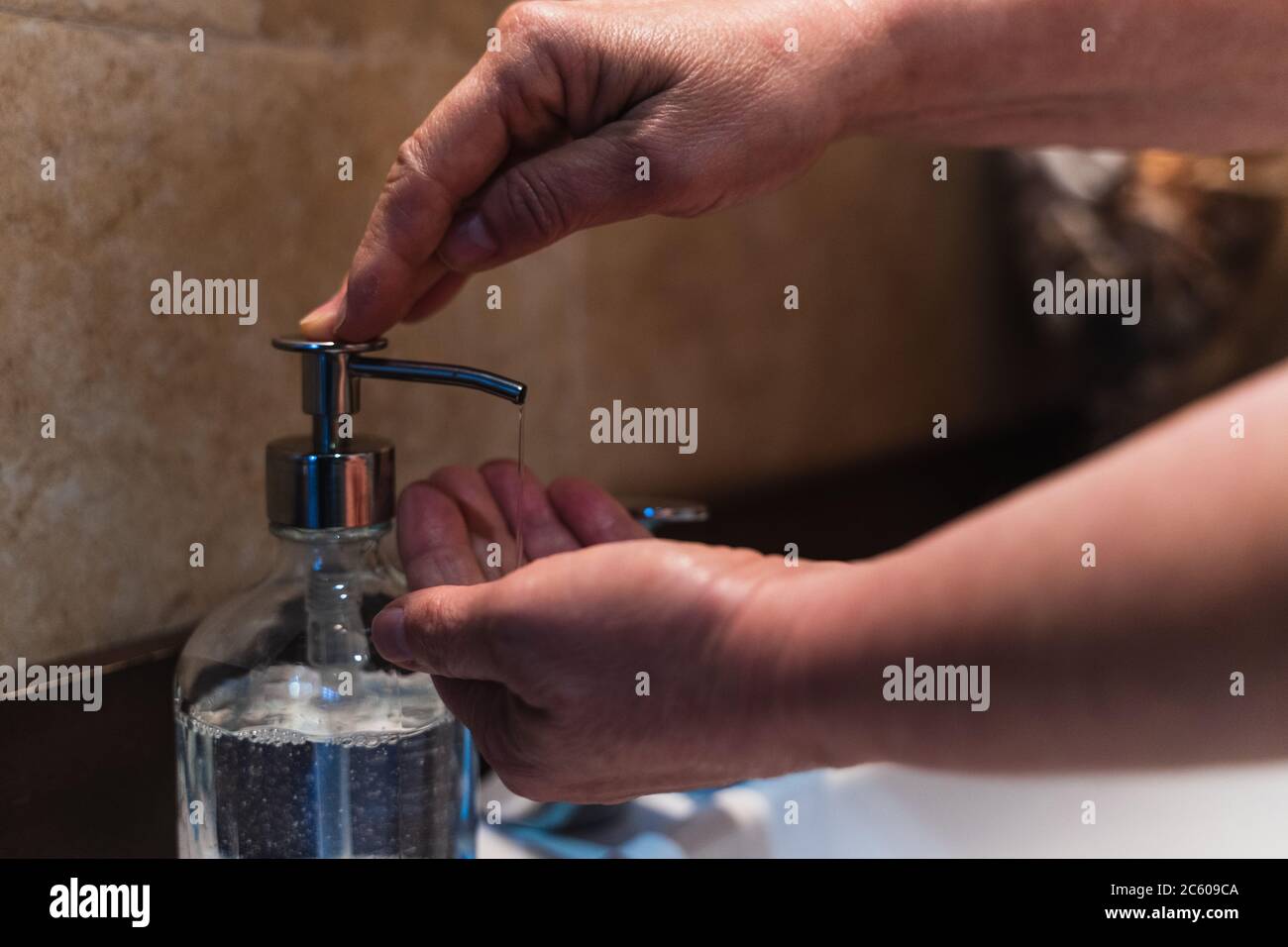 Person pressing a soap dispenser to wash hands on a white sink on a ...