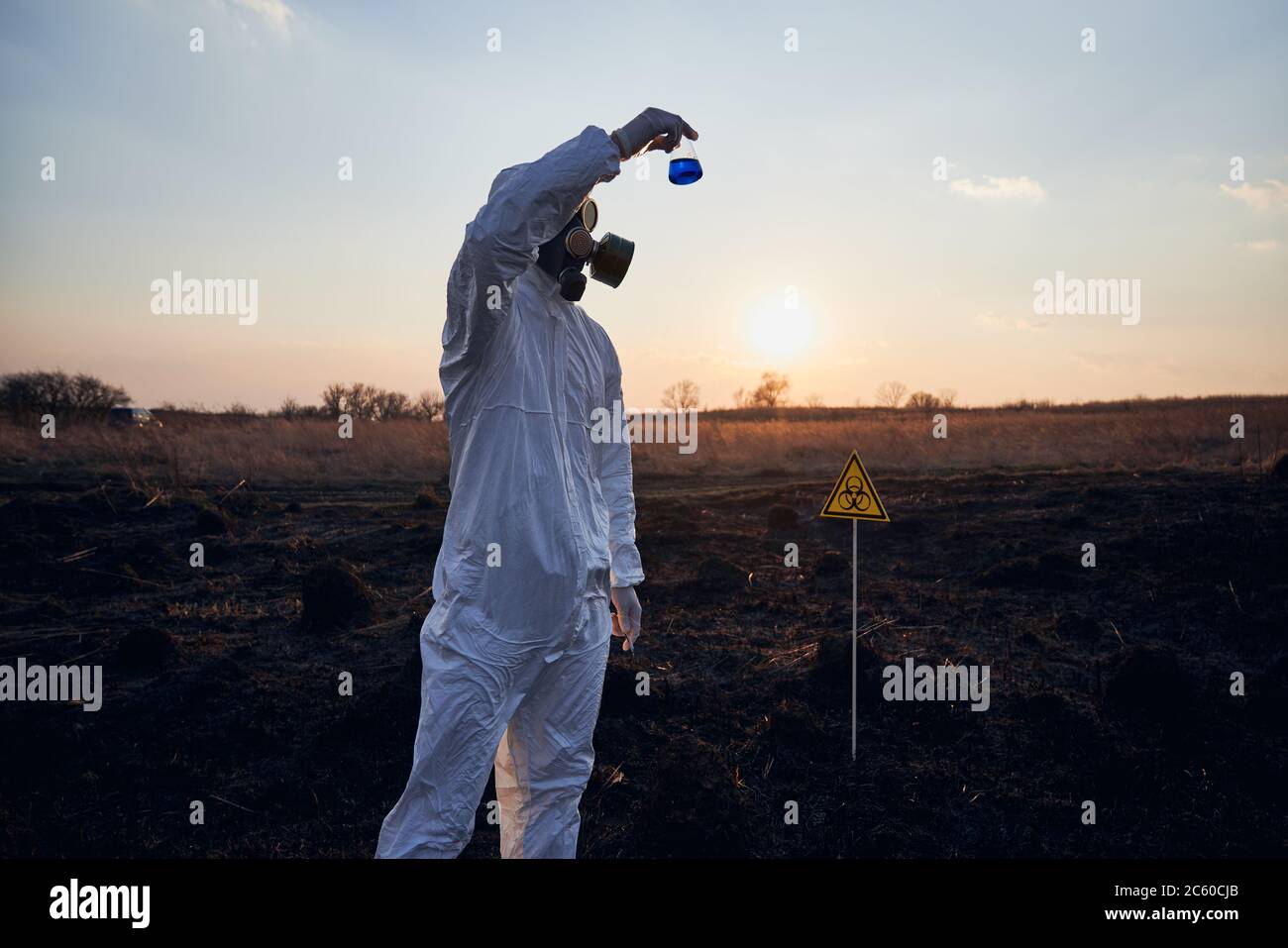 Male ecologist in radiation suit, gas mask holding test tube with blue ...