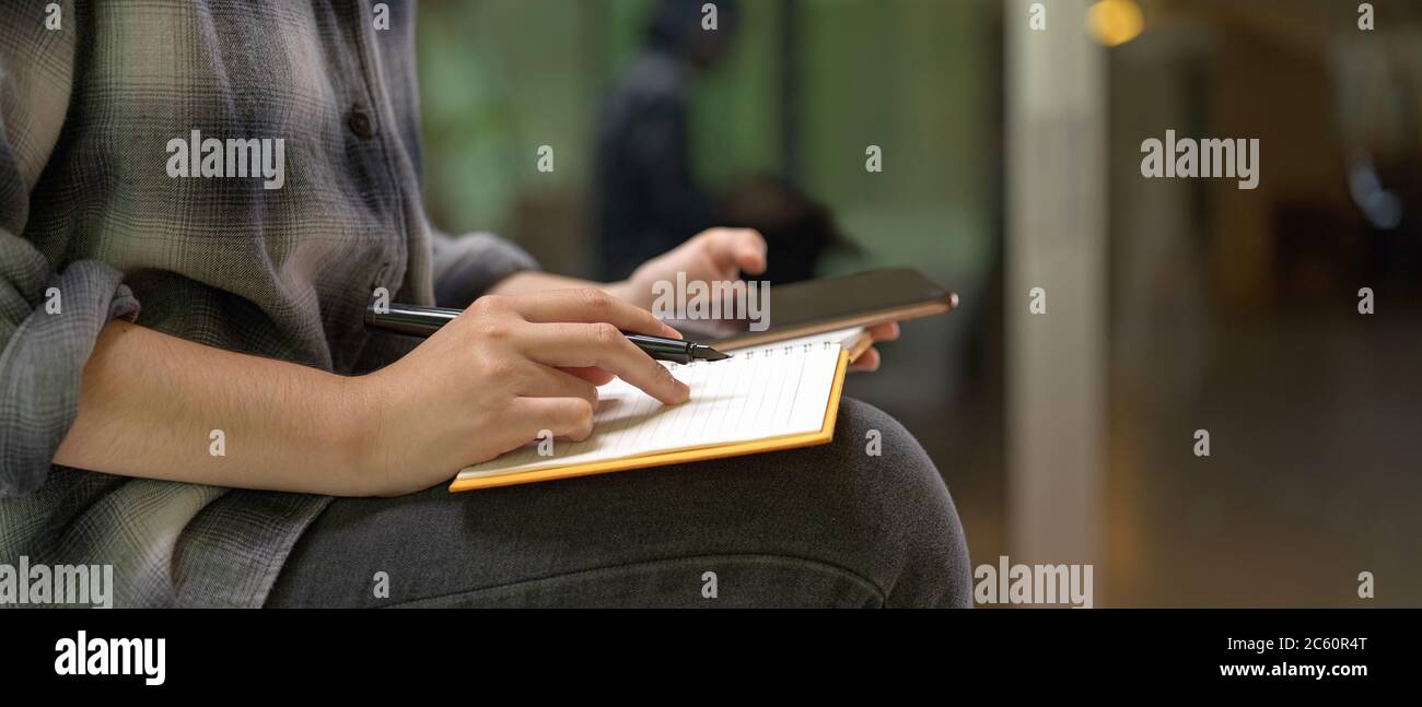 Side view of female worker sitting on worktable and taking note on ...