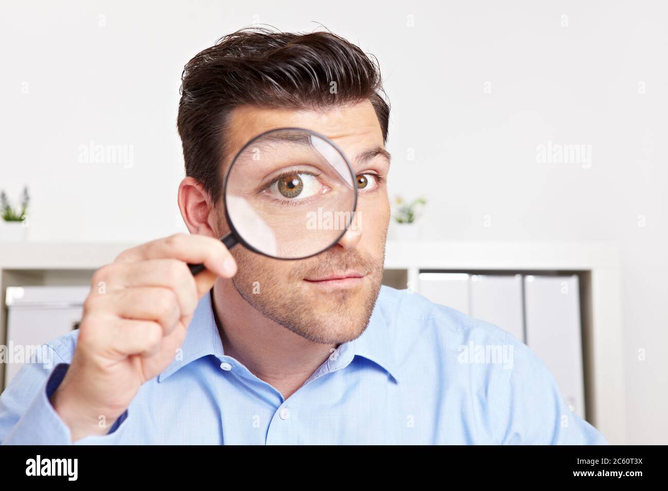 Attractive manager in the office looks through a magnifying glass with ...