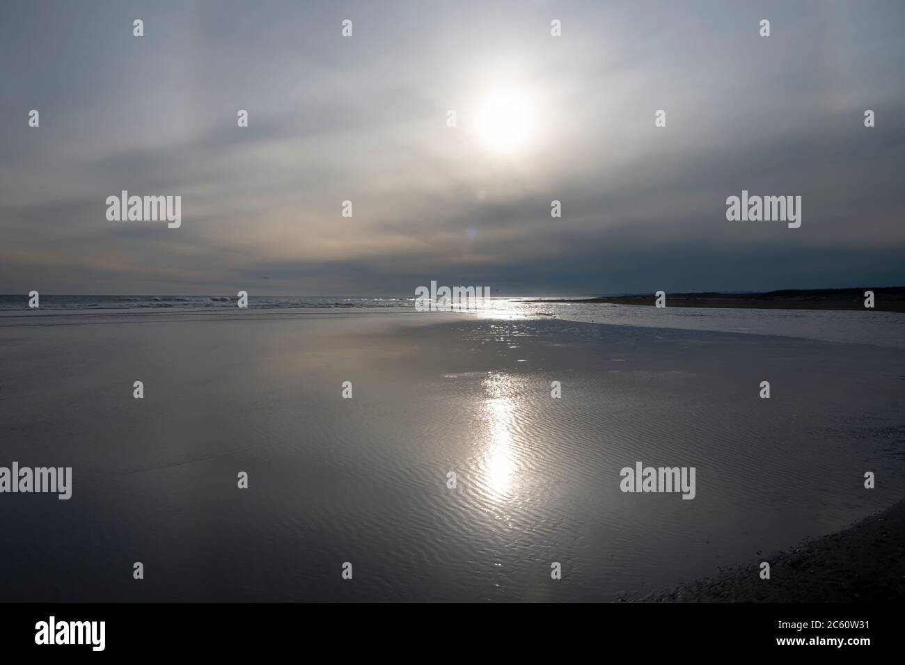 Diffused sun shining through clouds and reflected in beach and sea ...