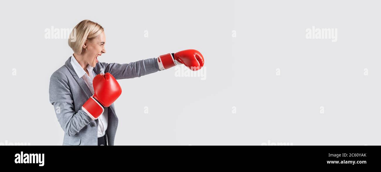 Side view of business lady in boxing gloves throwing punch on light ...