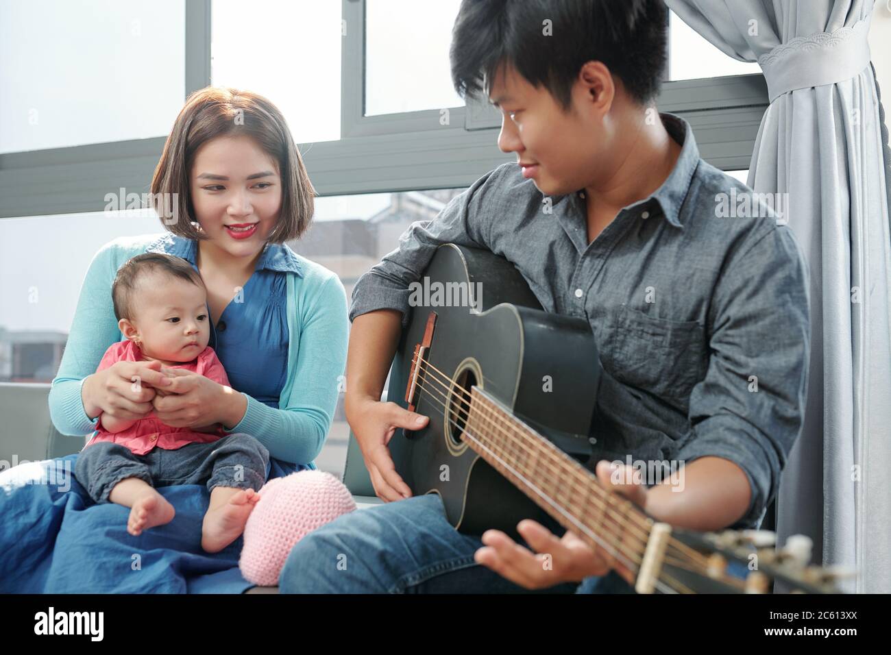 Vietnamese young man playing guitar and singing for his little daughter ...