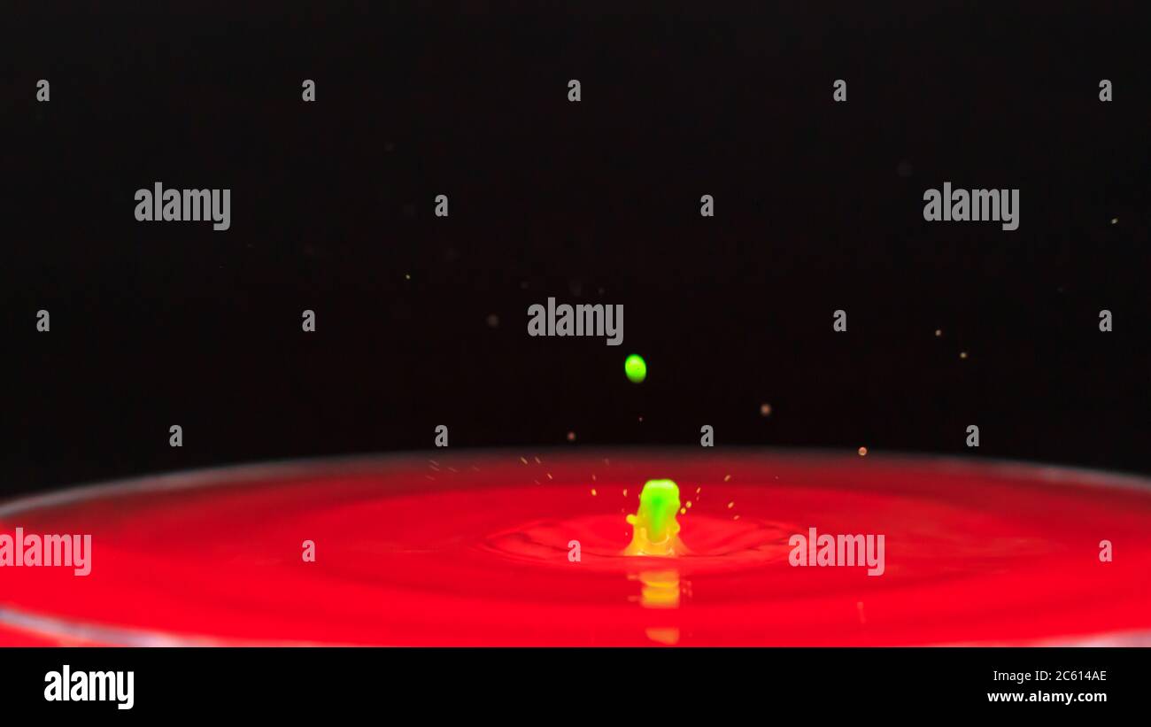 Green color drop falling in red water,contrast colors Stock Photo - Alamy