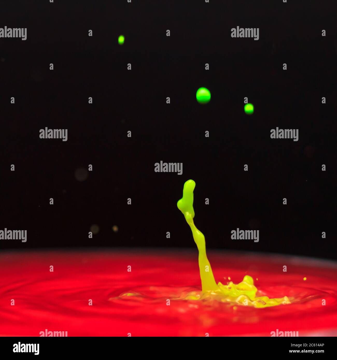 Green color drop falling in red water,contrast colors Stock Photo - Alamy