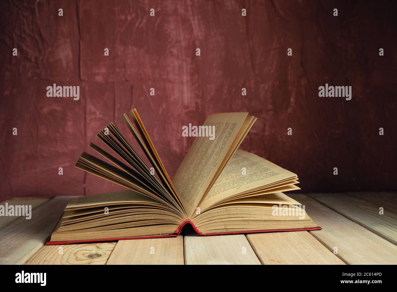 Beautiful ancient open old book on a red wooden table and dark-red wall ...