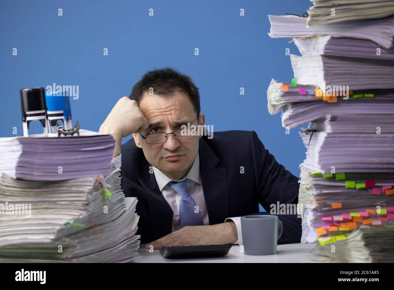 sad depressed businessman sitting at office desk with huge stack of ...