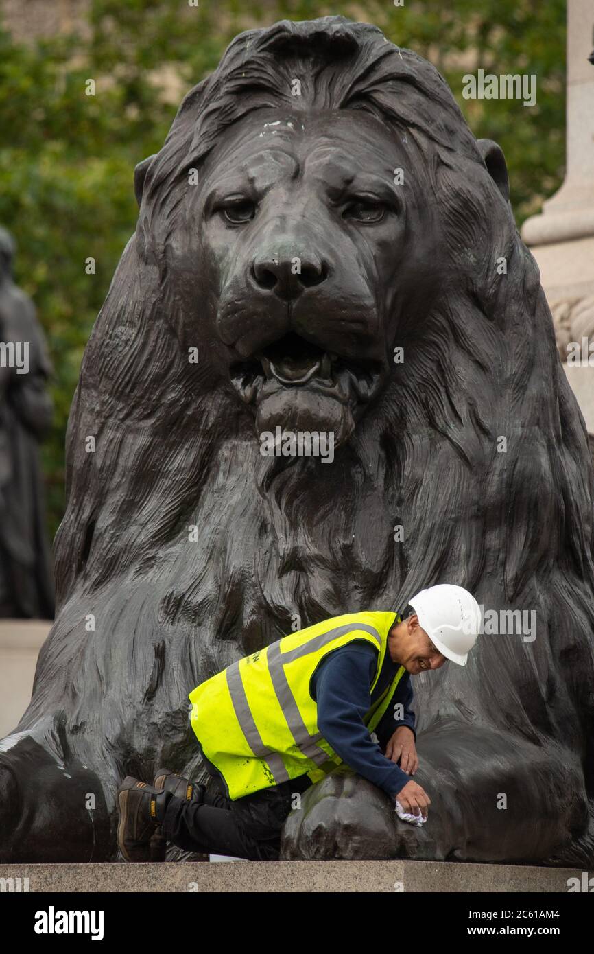A worker cleans and polishes one of the four lion statues at the base ...