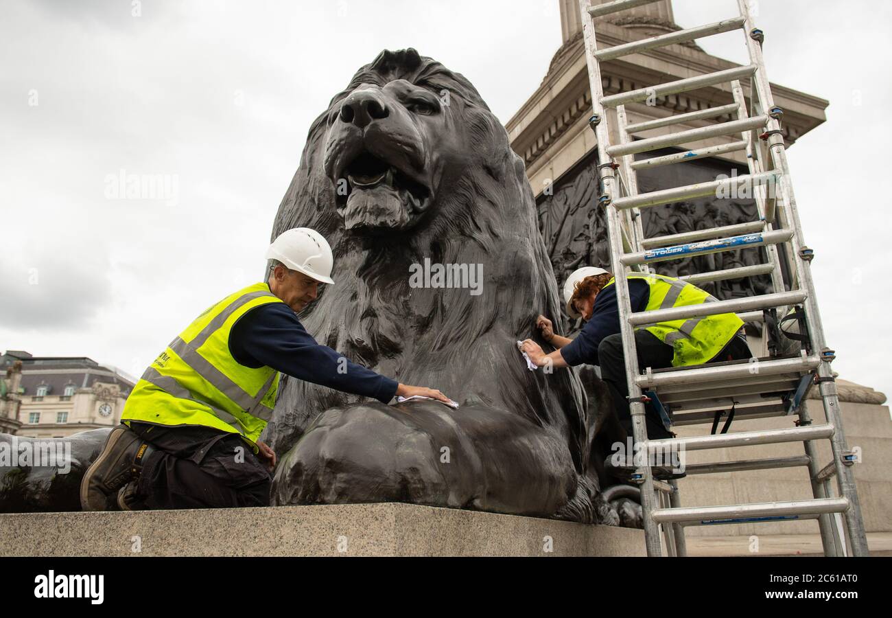 Workers clean and polish one of the four lion statues at the base of ...