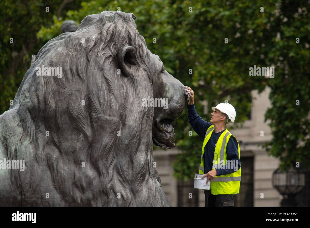 A worker cleans and polishes one of the four lion statues at the base ...