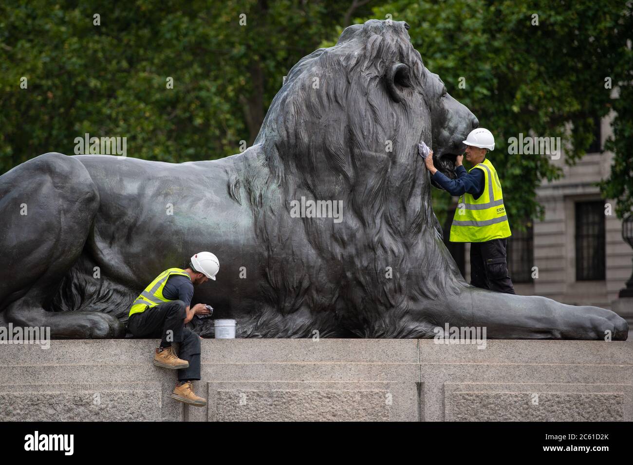 Workers clean and polish one of the four lion statues at the base of ...