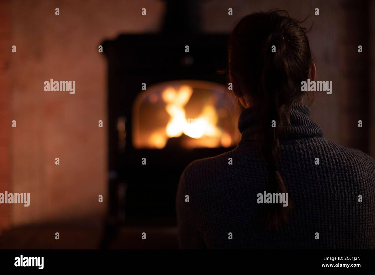 back view of brunette girl in gray sweater looking at fireplace in ...