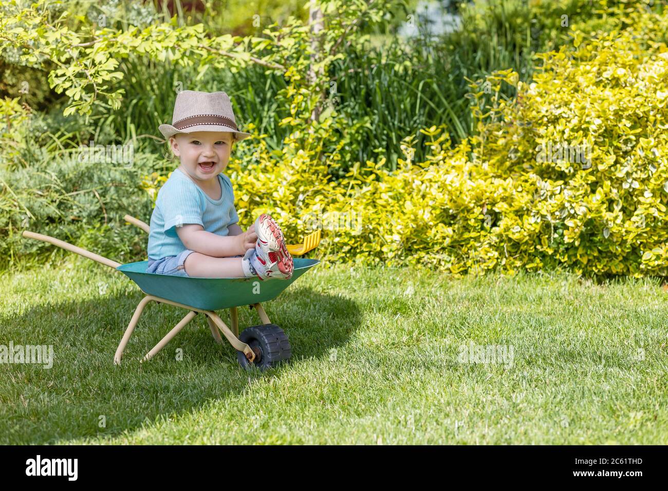 Cute baby boy is smiling at the camera sitting on green wheelbarrow in ...