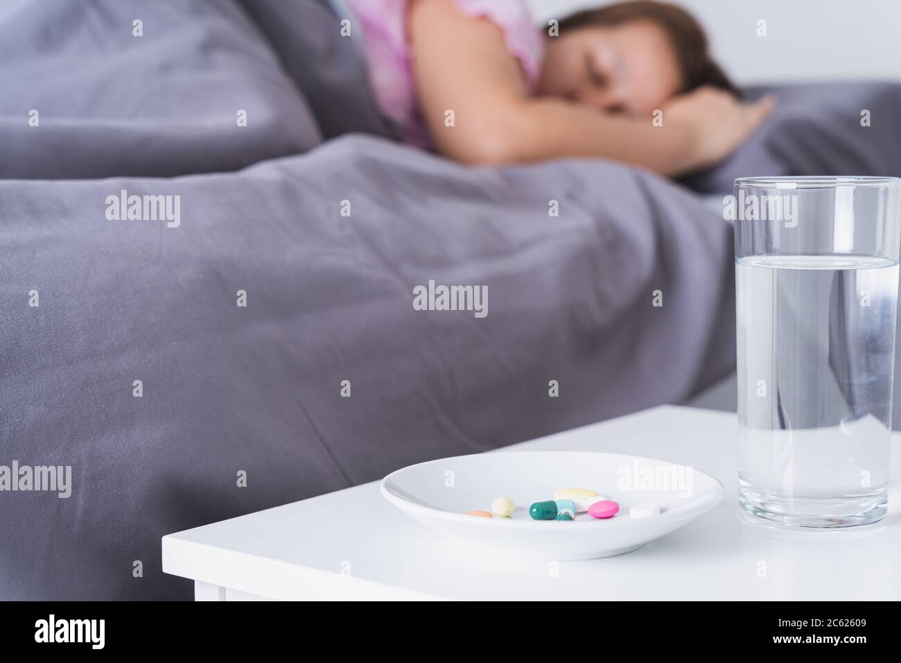 Close up pill drugs in the dish and a glass of water on nightstand and ...