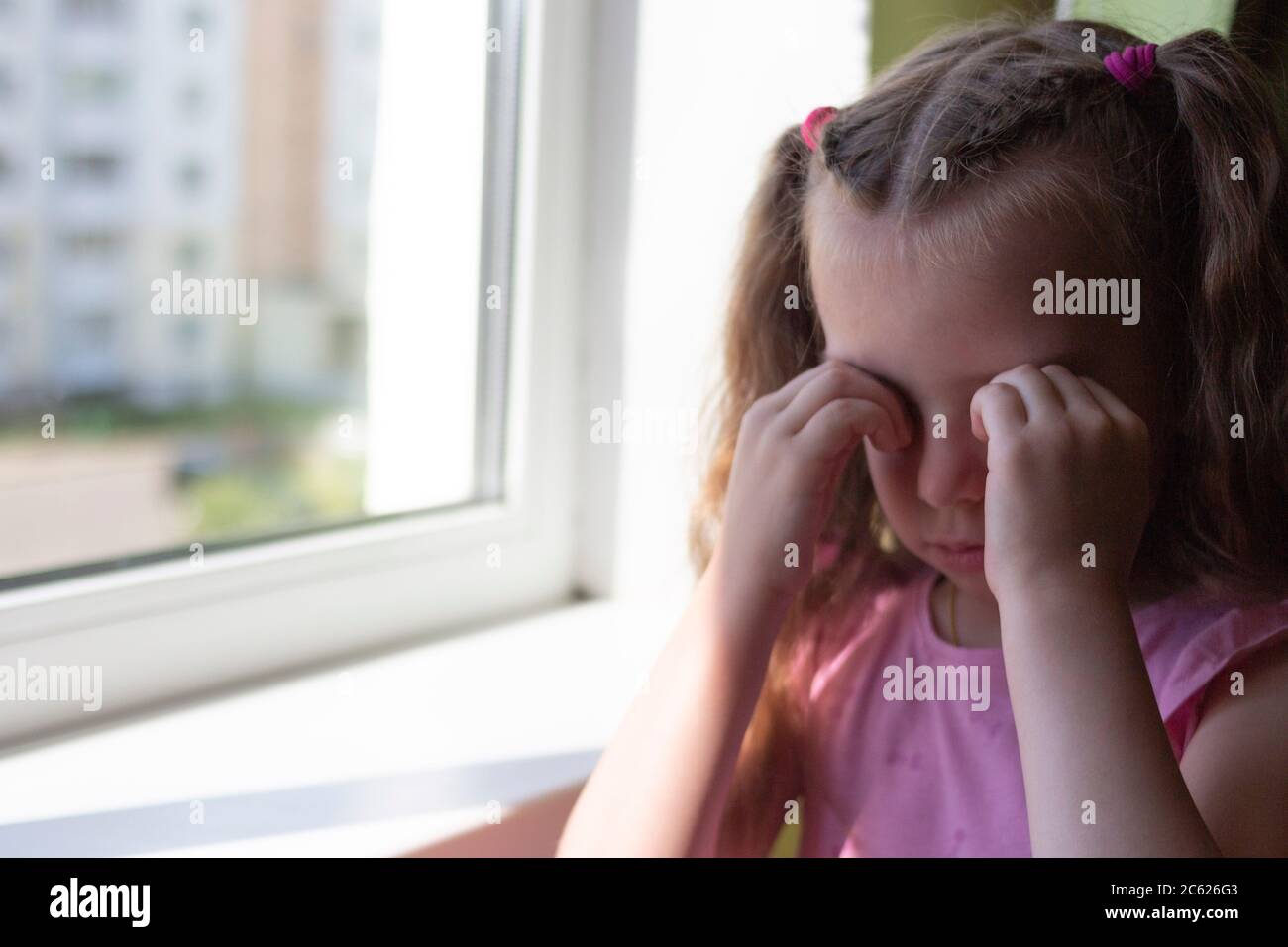 a small child cries and closes his eyes, standing by the window Stock ...