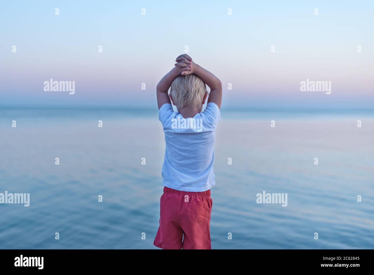 blond boy stands on sea background and sunset. Calm and relax concept ...