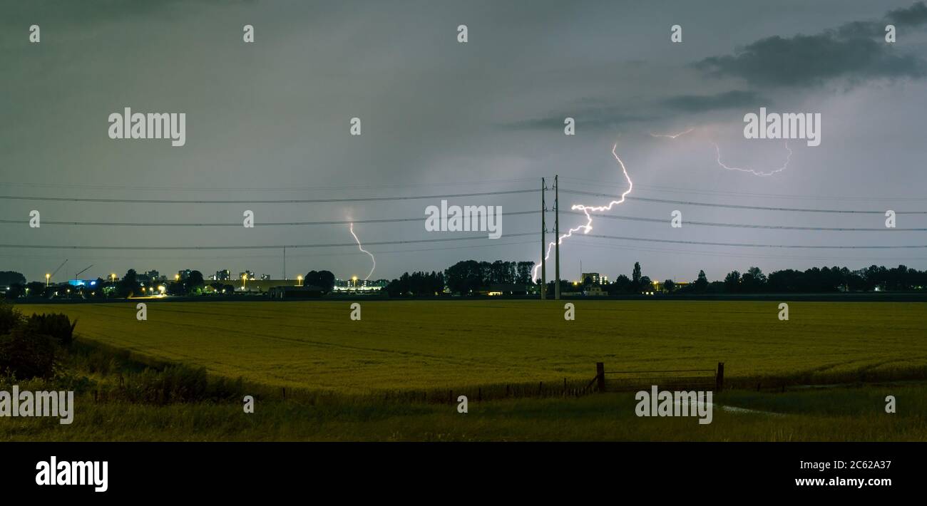 Bolt of lightning is hitting the ground near power lines during a ...
