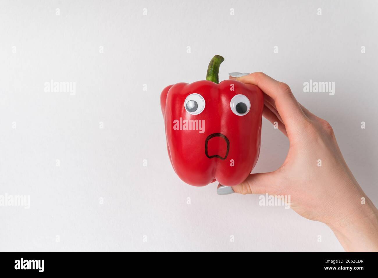 Hand holds red bell paprika with Googly eyes and frightened funny face ...