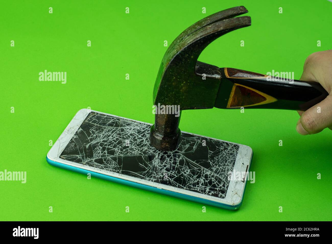 Hand holding Hammering the phone smartphone screen is cracked on green ...