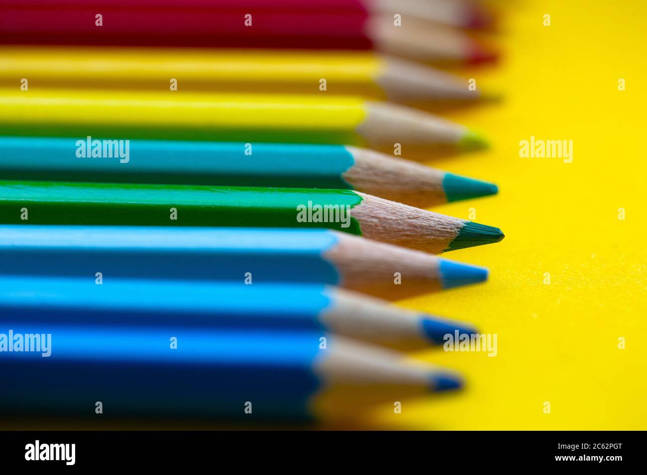 Colored pencils in the colors of rainbow in a row on a yellow ...